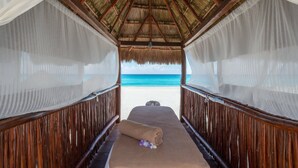 Quarto à beira-mar com telhado de palha, cama com toalha e vista para o oceano.