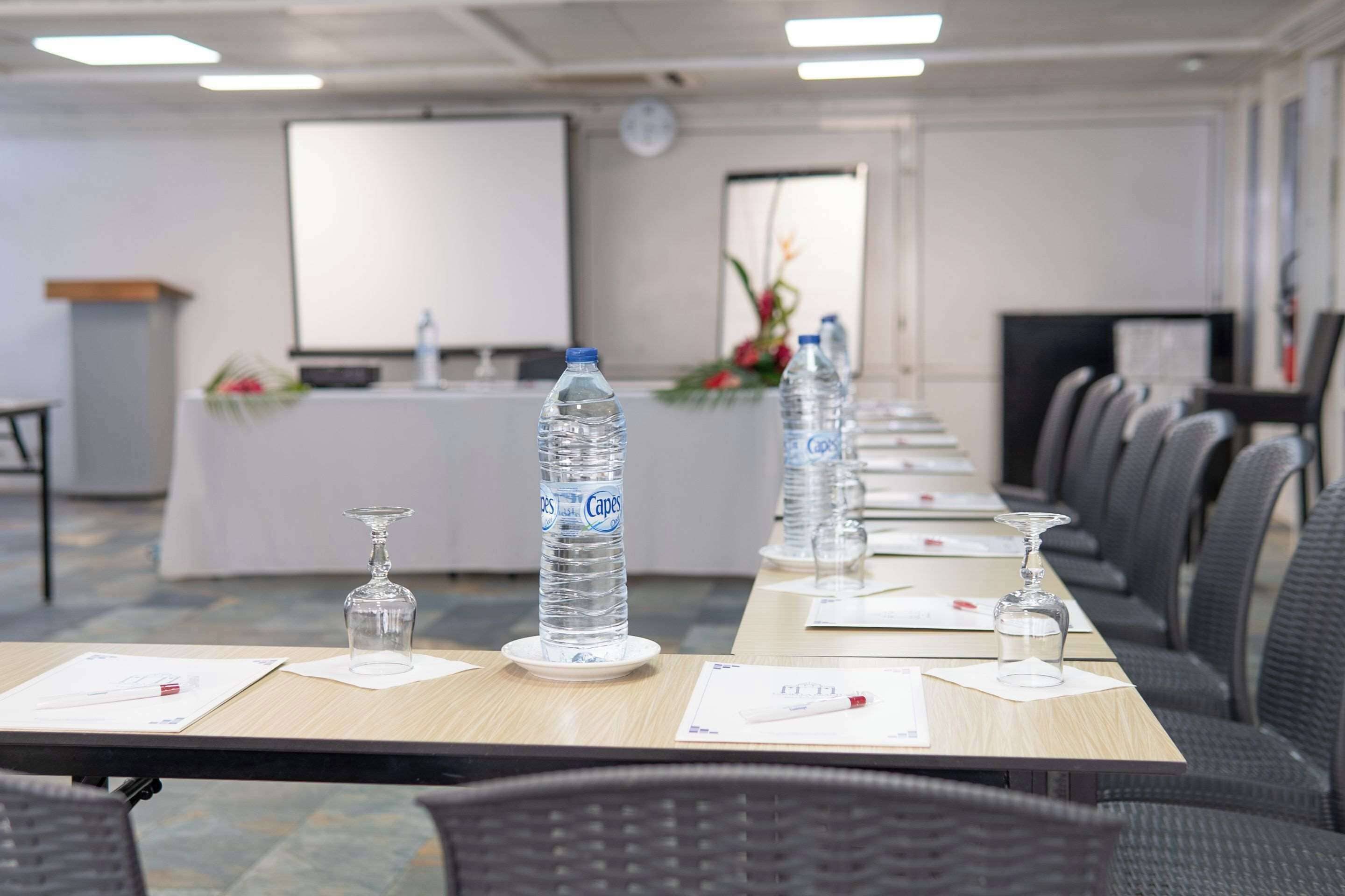 Uma sala de conferências com uma mesa comprida, garrafas de água e copos de vinho.