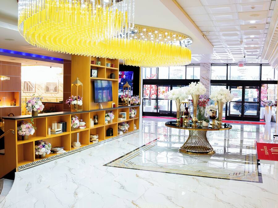 Um hall de entrada com piso de mármore, um lustre imponente e um balcão de recepção com estantes de livros e flores.
