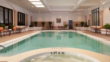 Piscina interna com profundidade de 1,47 metros, cercada por espreguiçadeiras e mesas, com paredes de tijolo e grandes janelas.
