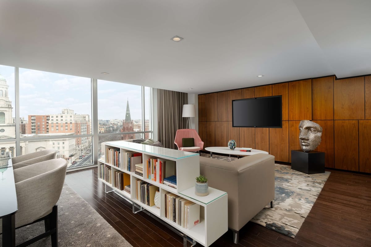 Uma sala de estar moderna com uma janela grande, uma estante de livros, um sofá, uma mesa de centro e uma televisão de tela plana.