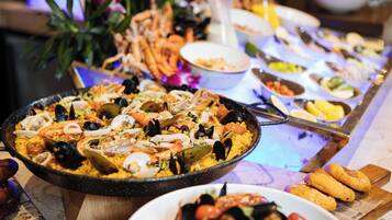 Um buffet de frutos do mar com diversos pratos, incluindo camarão, mexilhões e uma paella grande.
