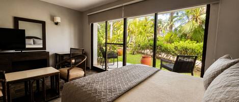 Quarto com uma cama grande, uma escrivaninha, uma cadeira e uma televisão. Há uma janela com vista para o verde lá fora.