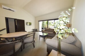 Uma sala de estar moderna com área de jantar, sofá, mesa de centro e uma grande janela com vista para o verde.