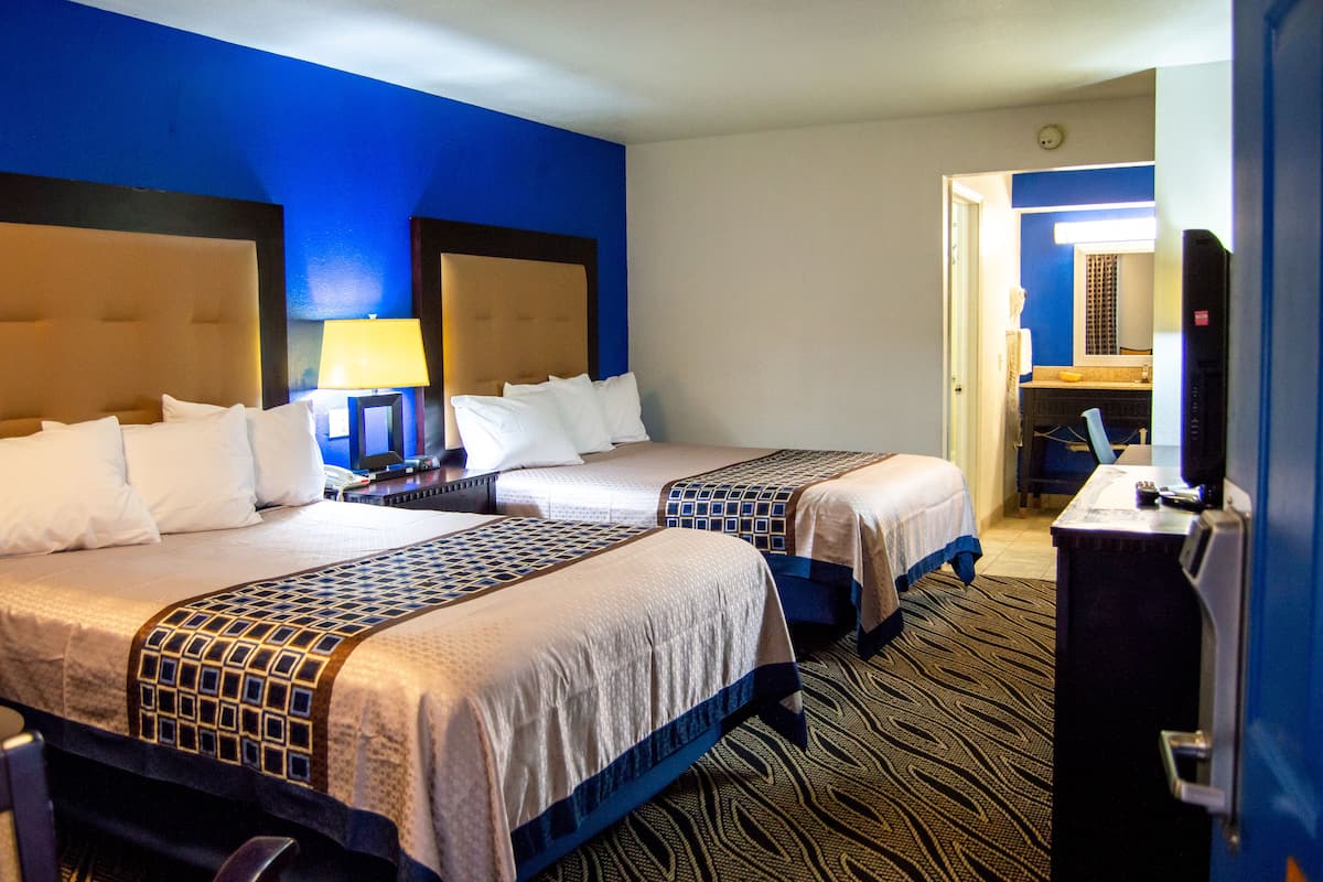 Quarto de hotel com duas camas, uma escrivaninha e um banheiro visível por uma porta aberta.