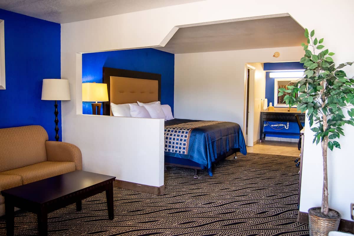 Quarto de hotel com cama, sofá, escrivaninha e planta em vaso.