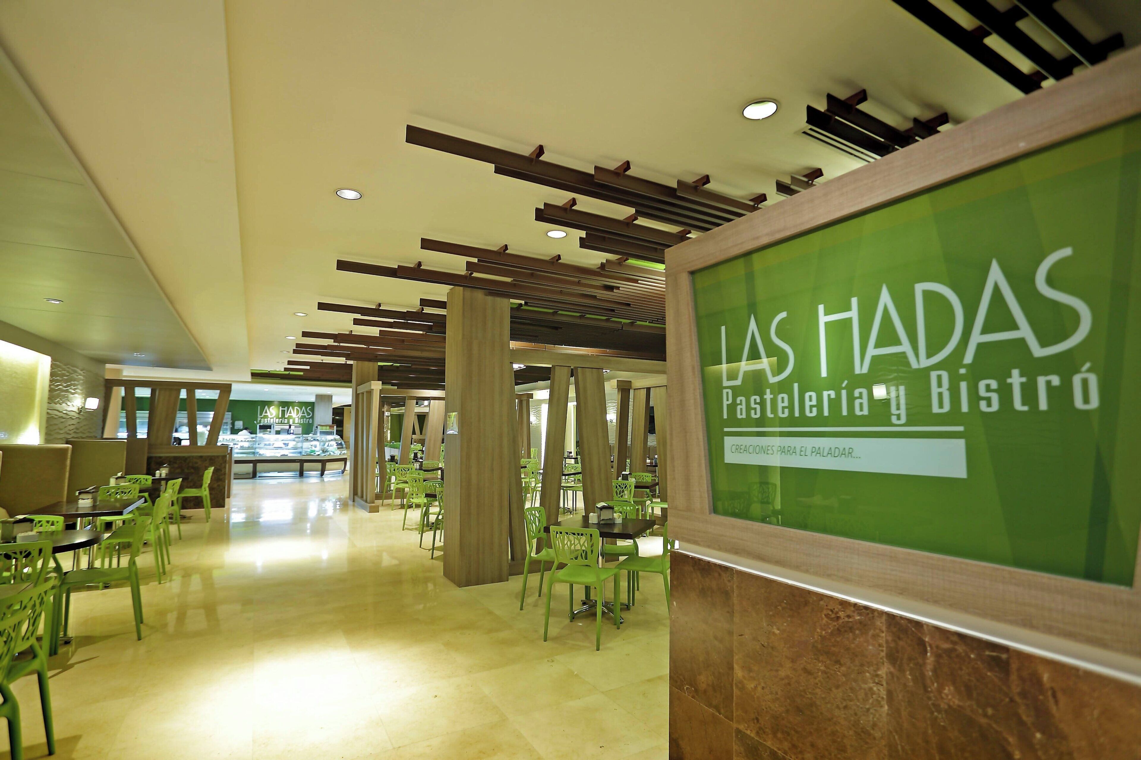 Um restaurante com cadeiras e mesas verdes, um letreiro com a inscrição 'Las Hadas Pastelería y Bistrot', e um chão de mármore.