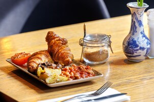 Prato de café da manhã com croissants, tomates, feijão e batatas em uma mesa de madeira.