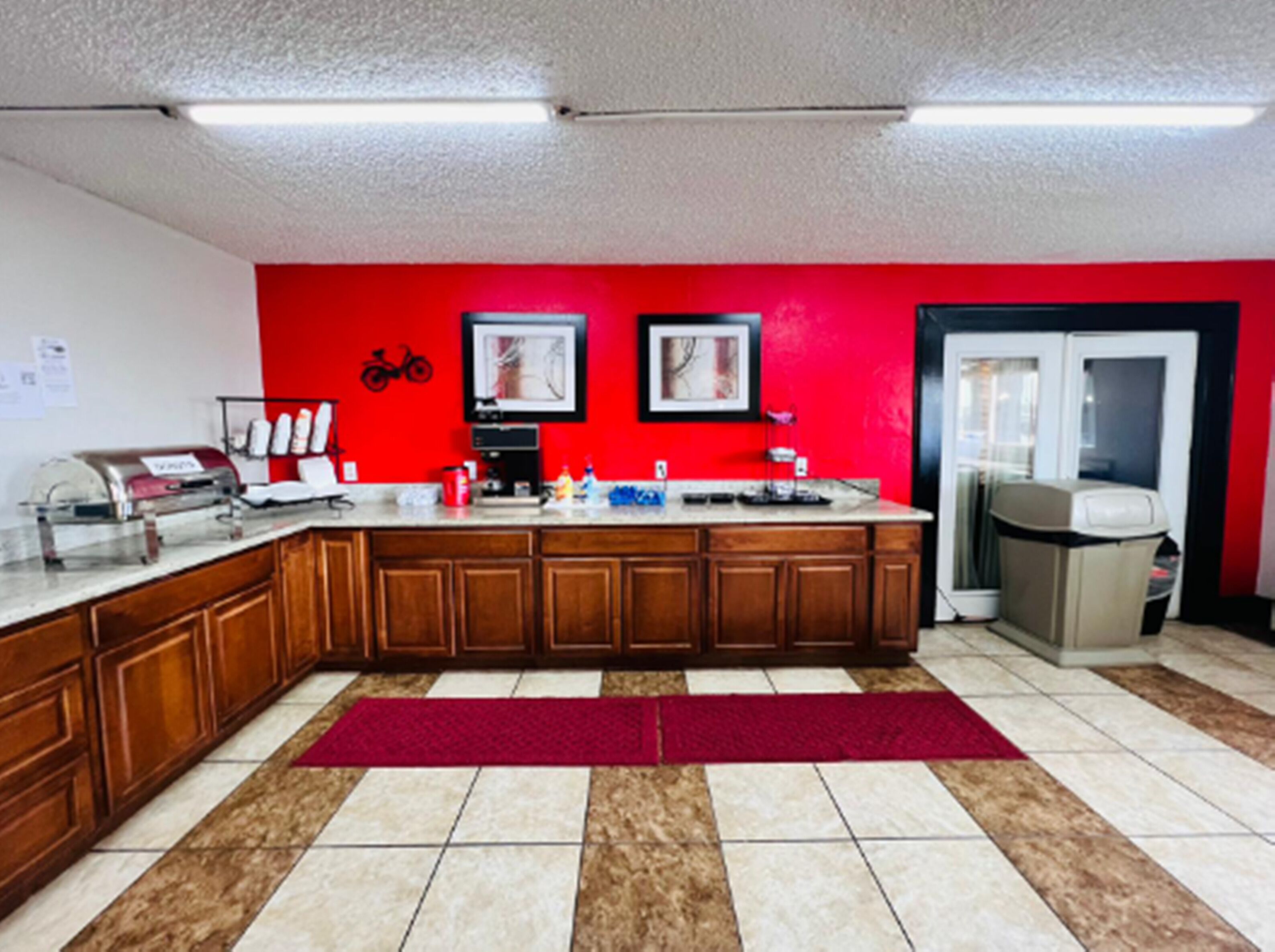 Uma cozinha com parede vermelha, armários de madeira, bancada de mármore e tapete vermelho.