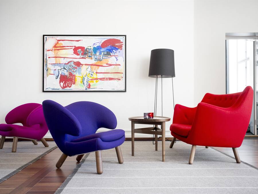 Quarto moderno com três poltronas vibrantes, um abajur preto e uma pintura abstrata colorida na parede.