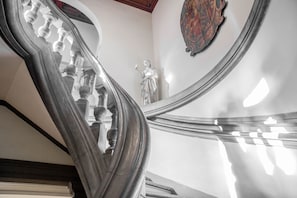Uma escadaria imponente com grades ornamentadas e uma estátua ao fundo.