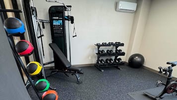 Academia com banco, anilhas, halteres, bola medicinal e bicicleta ergométrica.