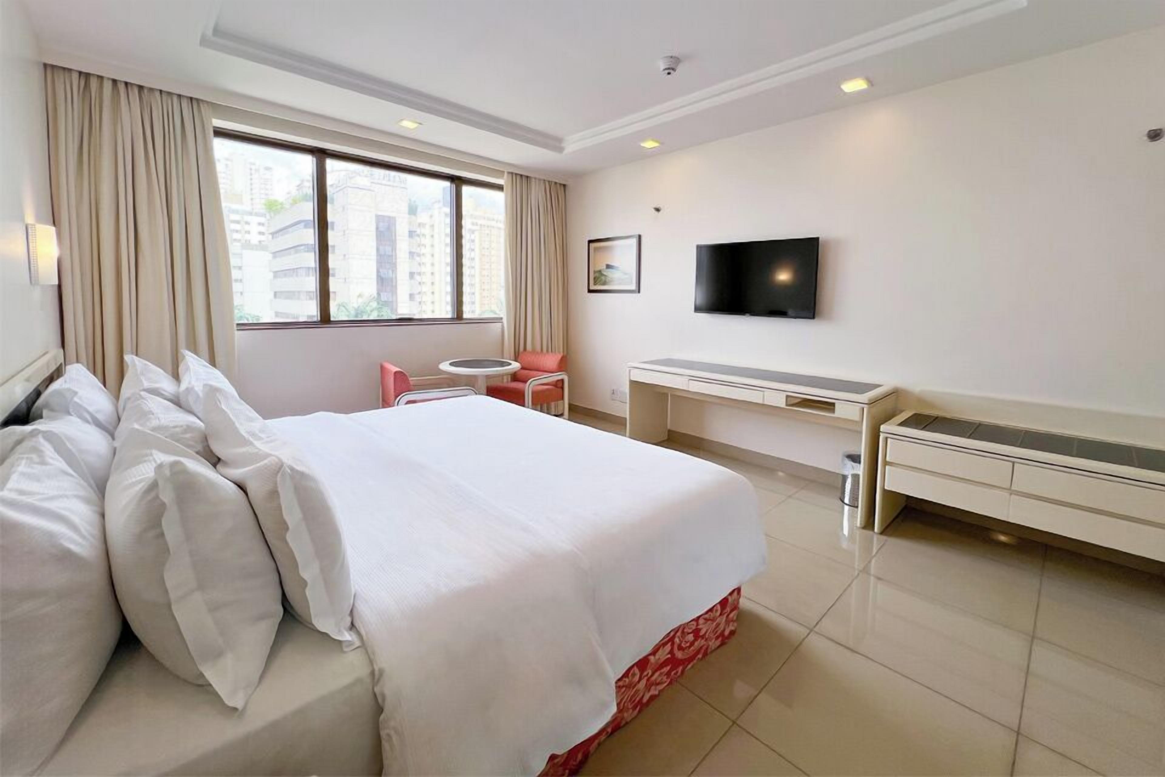 Quarto de hotel com uma cama grande, uma escrivaninha, uma cadeira, uma televisão e uma janela com cortinas.