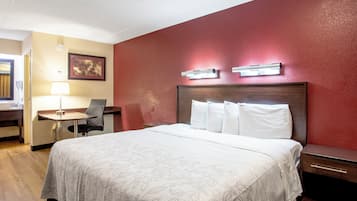 Quarto de hotel com cama, escrivaninha, cadeira e luminária na parede.