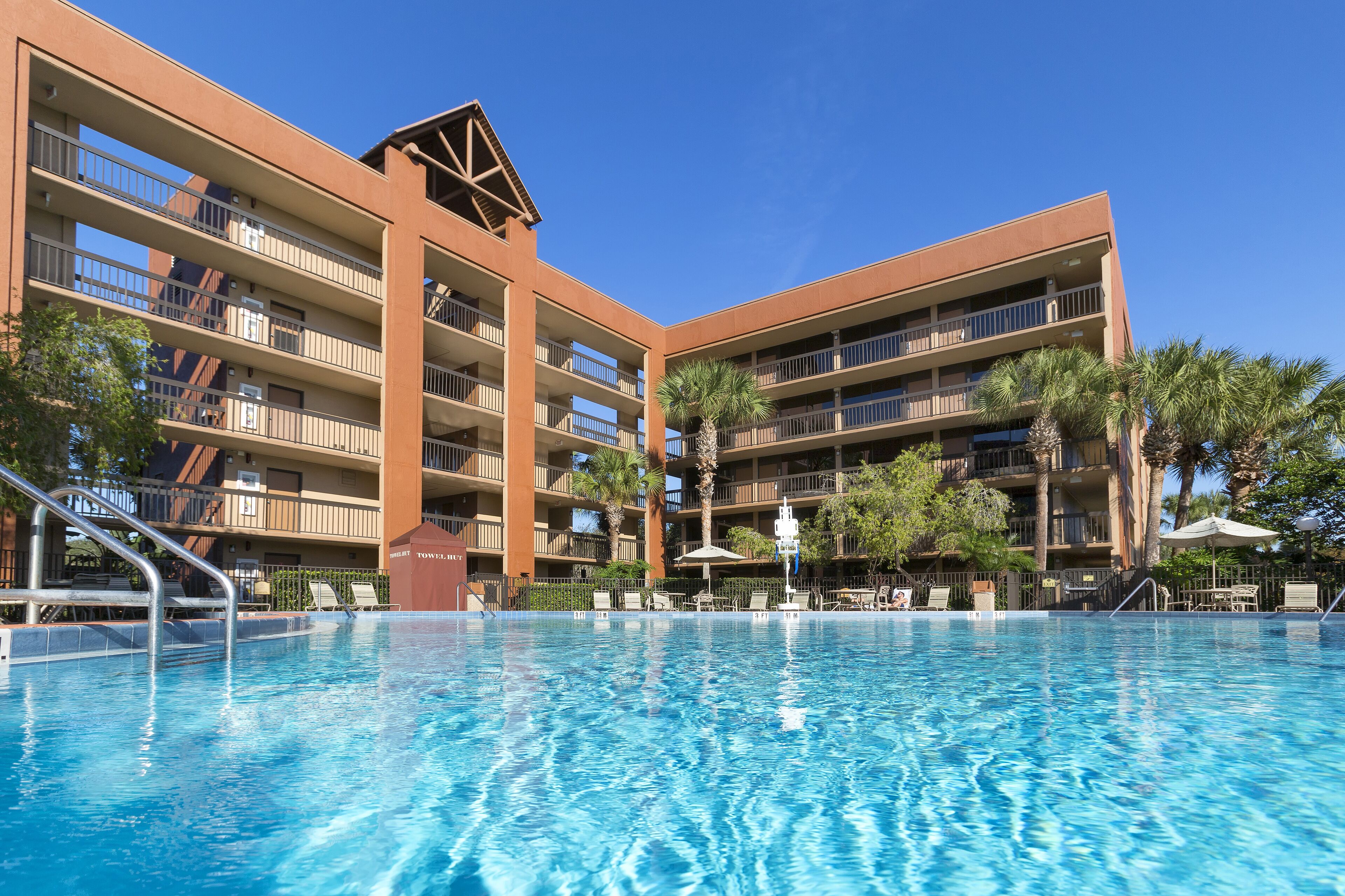 Um hotel com piscina, várias varandas e palmeiras.