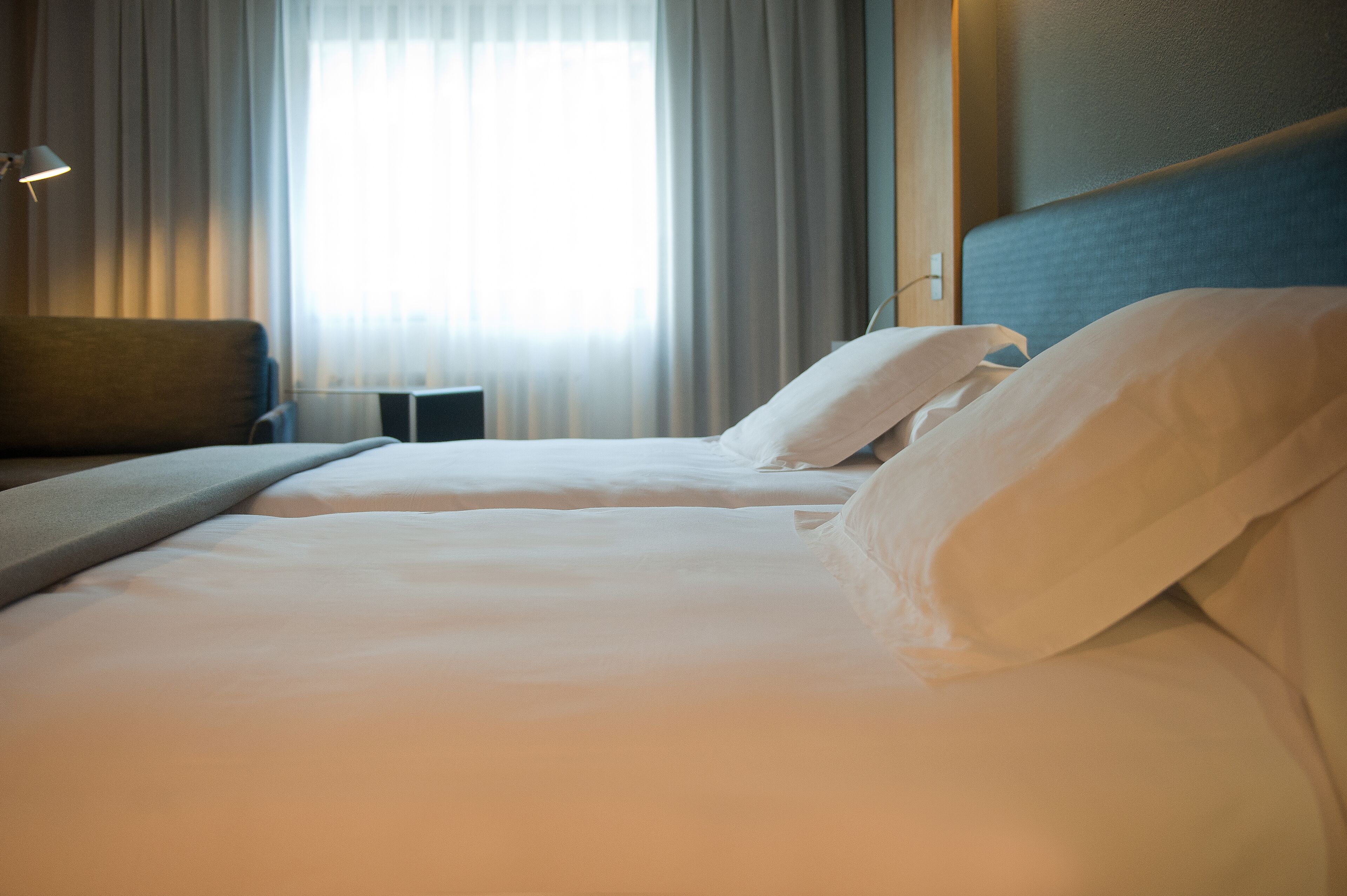 Quarto de hotel com uma cama bem arrumada, uma mesa de cabeceira e uma luminária.