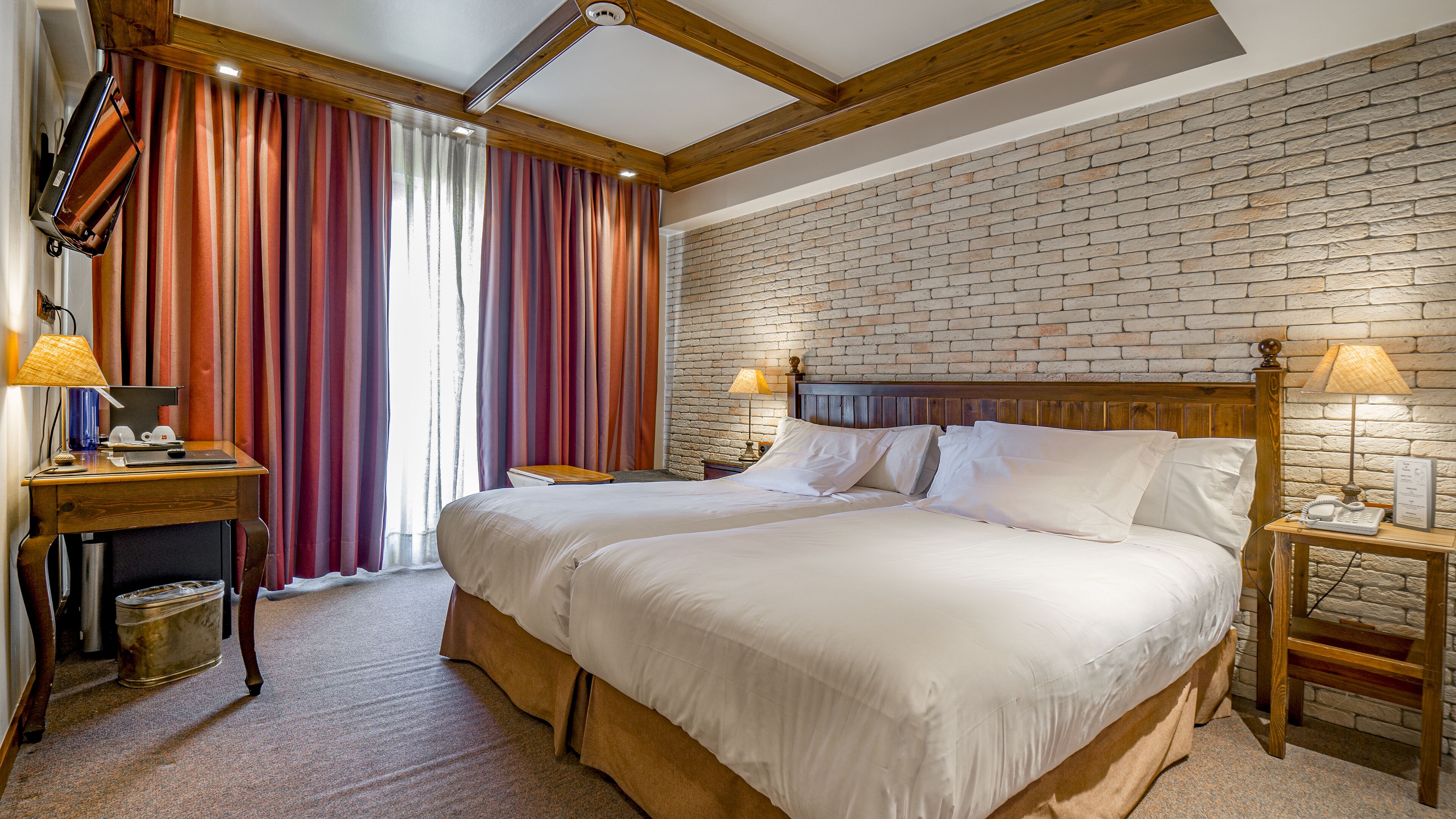 Quarto de hotel com uma cama grande, uma mesa de trabalho com abajur e uma parede de tijolos.
