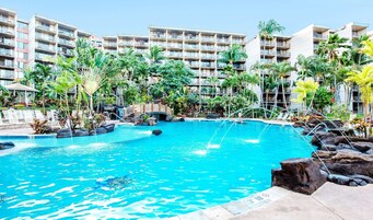 Piscina de hotel com águas azuis cristalinas, rodeada por palmeiras e um edifício alto com varandas.
