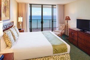 Quarto de hotel com uma cama grande, televisão, cadeira, cômoda e varanda com vista para o oceano.