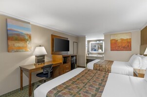 Quarto de hotel com escrivaninha, cadeira, duas camas, televisão e obras de arte nas paredes.