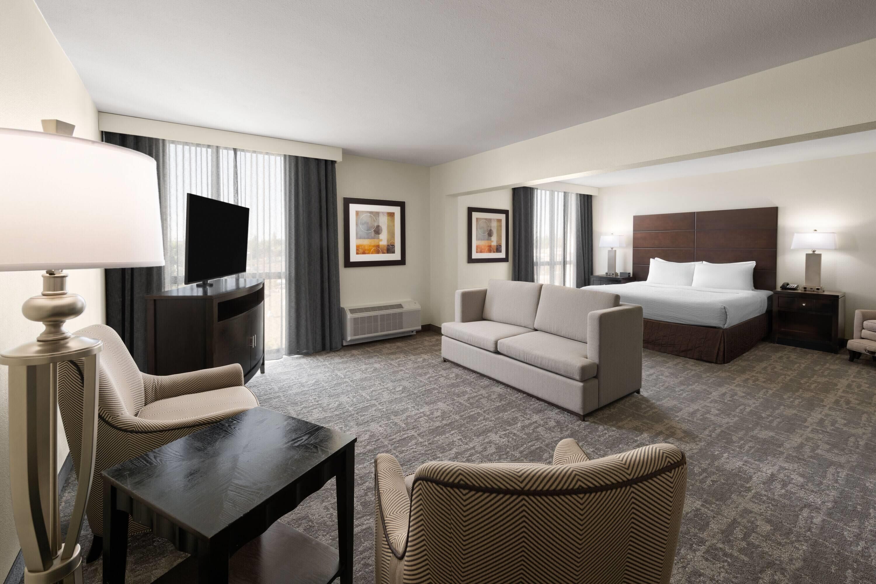 Quarto de hotel com cama, sofá, televisão, escrivaninha e cadeira.