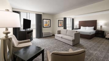 Quarto de hotel com cama, sofá, televisão, escrivaninha e cadeira.