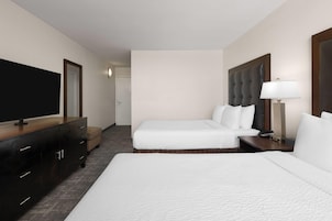 Quarto de hotel com duas camas, televisão, escrivaninha e luminária.
