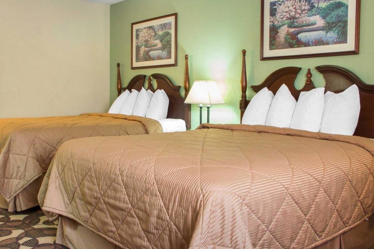 Quarto duplo com duas camas, uma luminária e duas fotografias emolduradas na parede.