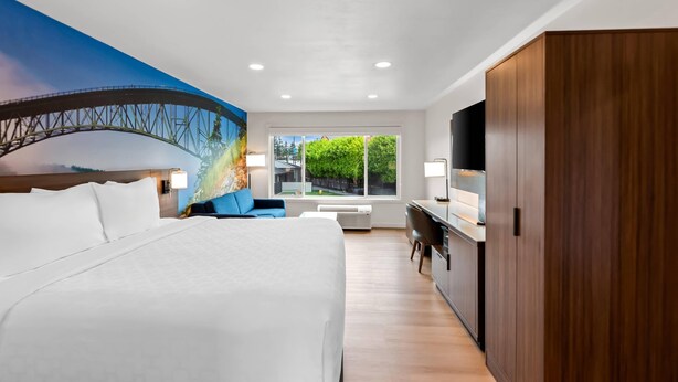 Quarto de hotel moderno com uma cama grande, escrivaninha, televisão e um mural de uma ponte.