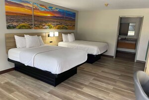 Quarto de hotel com duas camas, piso de madeira e uma grande pintura de paisagem acima das camas.
