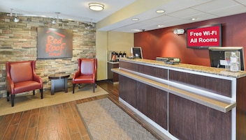 Área de recepção do Red Roof Inn, com parede de pedra, duas poltronas de couro, balcão de recepção e sinal indicando Wi-Fi gratuito em todos os quartos.