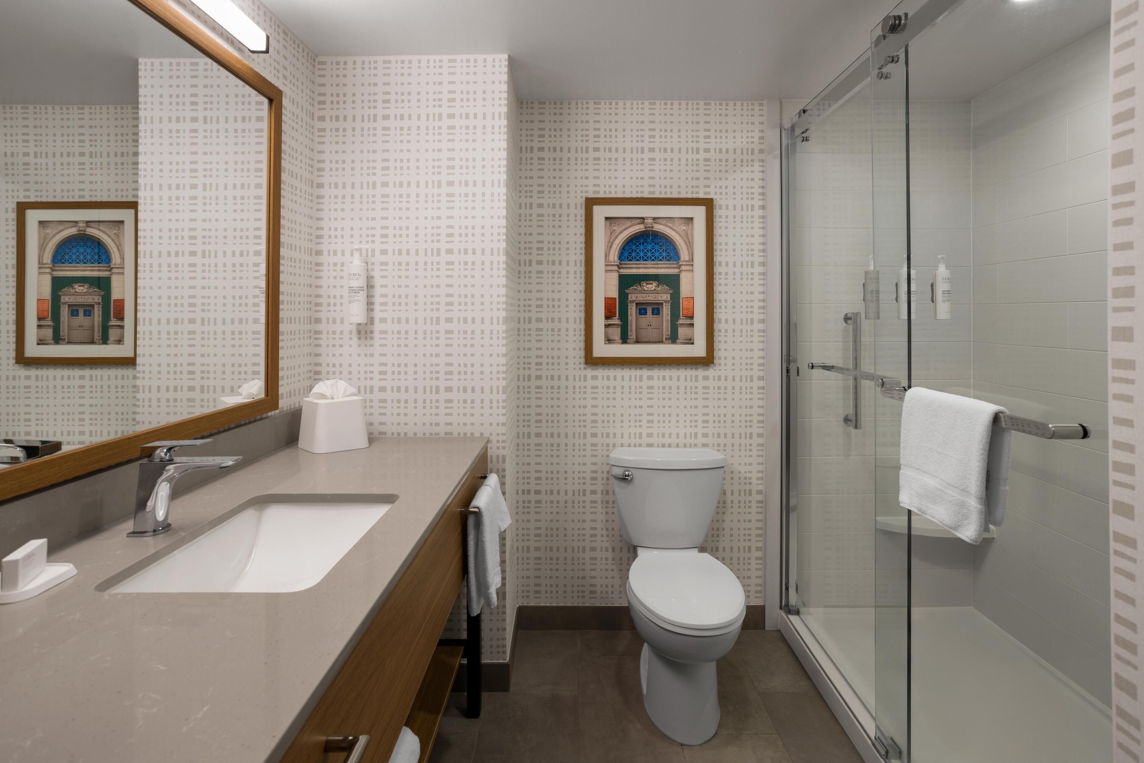 Uma casa de banho moderna com um espelho grande, lavatório, sanita e cabine de duche em vidro.