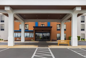 Entrada de hotel com galeria coberta, estacionamento e um banco.