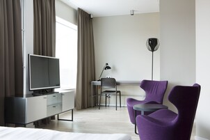 Quarto de hotel moderno com cama, escrivaninha com computador, cadeira, televisão e abajur.