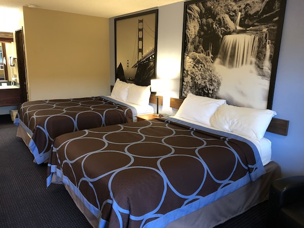 Quarto de hotel com duas camas, um espelho grande e duas fotos emolduradas na parede.