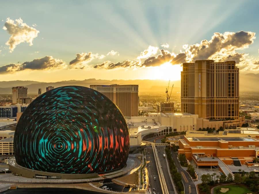 Um edifício esférico imponente com superfície refletora, rodeado por infraestrutura urbana e edifícios.
