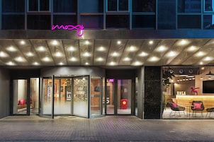 Entrada de hotel com porta de vidro, letreiro de neon e área de recepção com balcão e assentos.