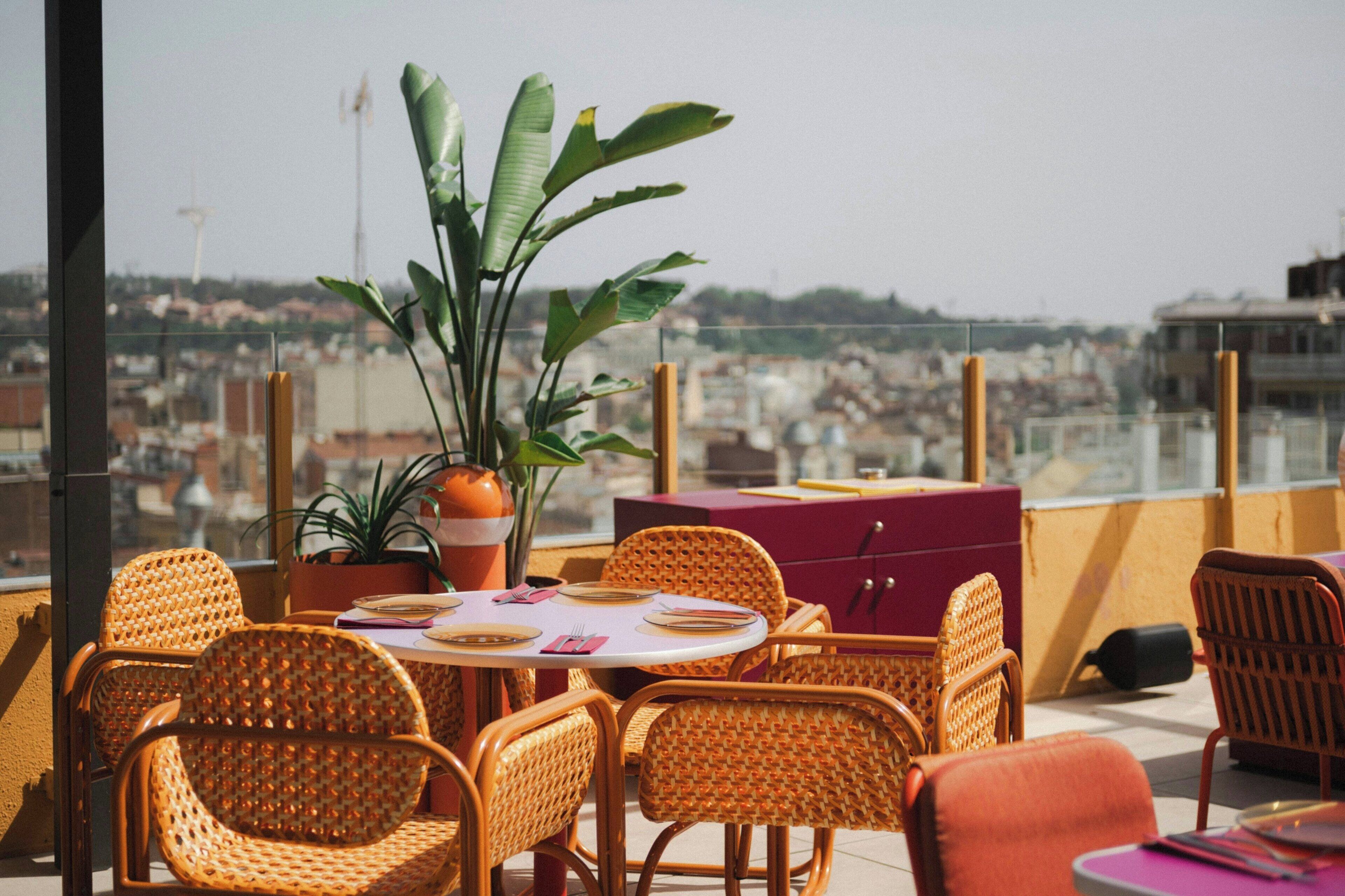 Terraço no telhado com cadeiras de vime e uma mesa posta para refeições, com vista para a paisagem urbana.
