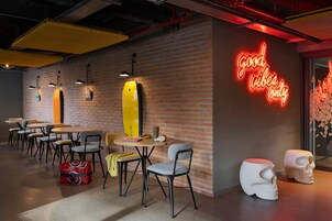 Um café moderno com paredes de tijolo, mesas e cadeiras de madeira, e um letreiro de neon que diz 'good vibes only'.