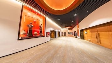 Corredor moderno de hotel com piso de madeira, uma vitrine central com artefatos e teto com design circular.
