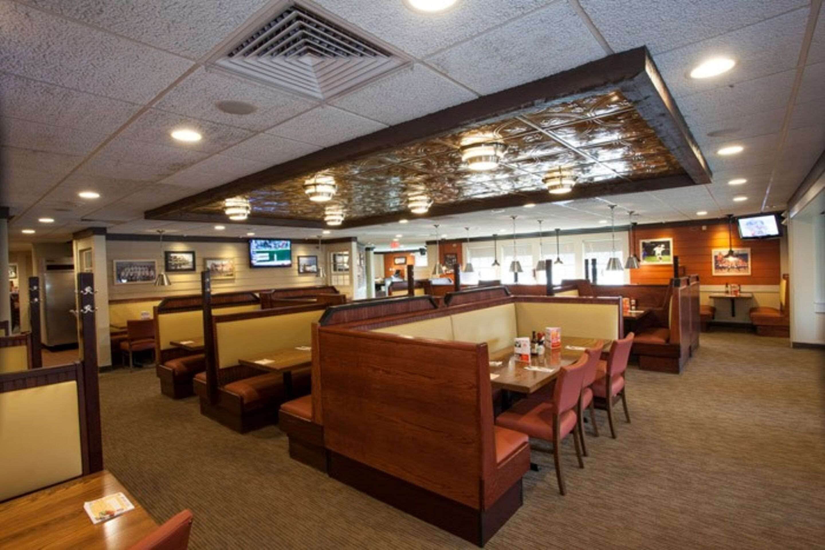Um restaurante com cabines e mesas, uma tela de televisão e um teto com design exclusivo.
