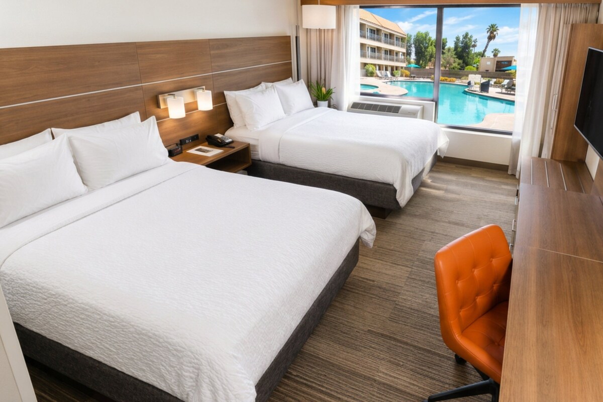 Quarto de hotel com duas camas, televisão, escrivaninha e vista para uma piscina.