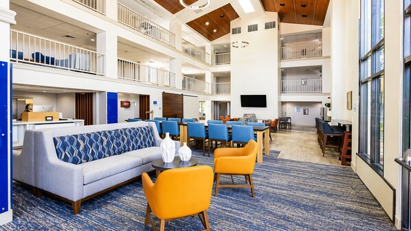 Um hall de hotel espaçoso, com teto alto, várias áreas de estar e uma mesa central.