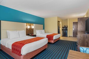 Quarto de hotel com duas camas, uma escrivaninha, uma cadeira, uma cozinha compacta e uma televisão.