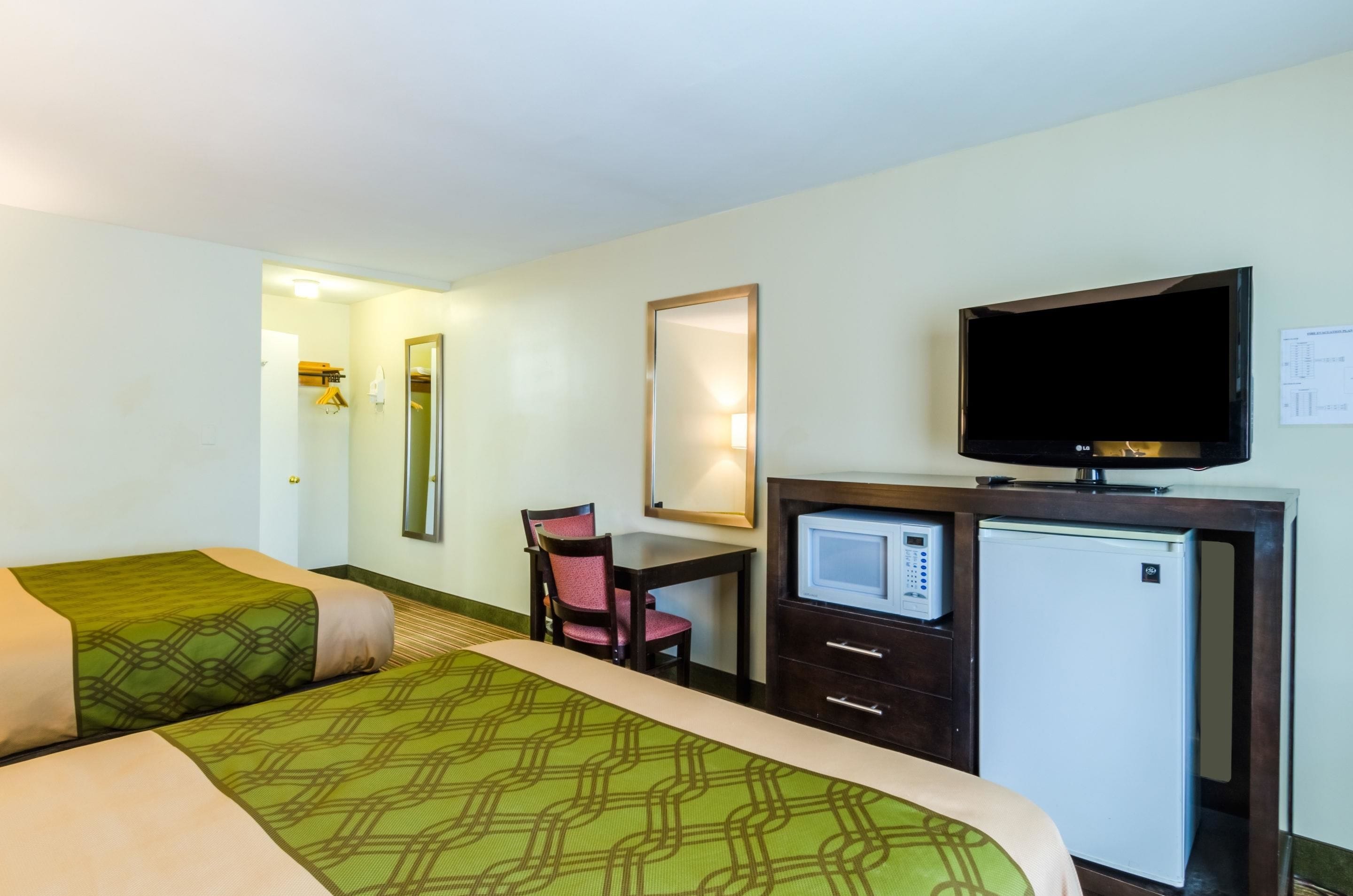 Quarto de hotel com duas camas, uma escrivaninha com cadeira, televisão, micro-ondas e frigorífico.
