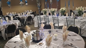 Salão de banquetes com mesas redondas preparadas para um evento formal, com talheres, guardanapos dobrados e arranjos florais.