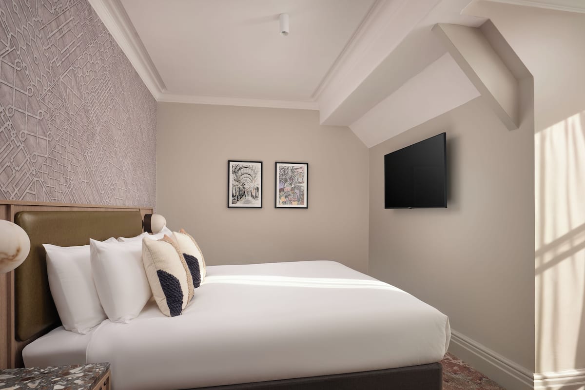 Um quarto bem arrumado com uma cama grande, uma TV de tela plana na parede e duas obras de arte emolduradas na parede.