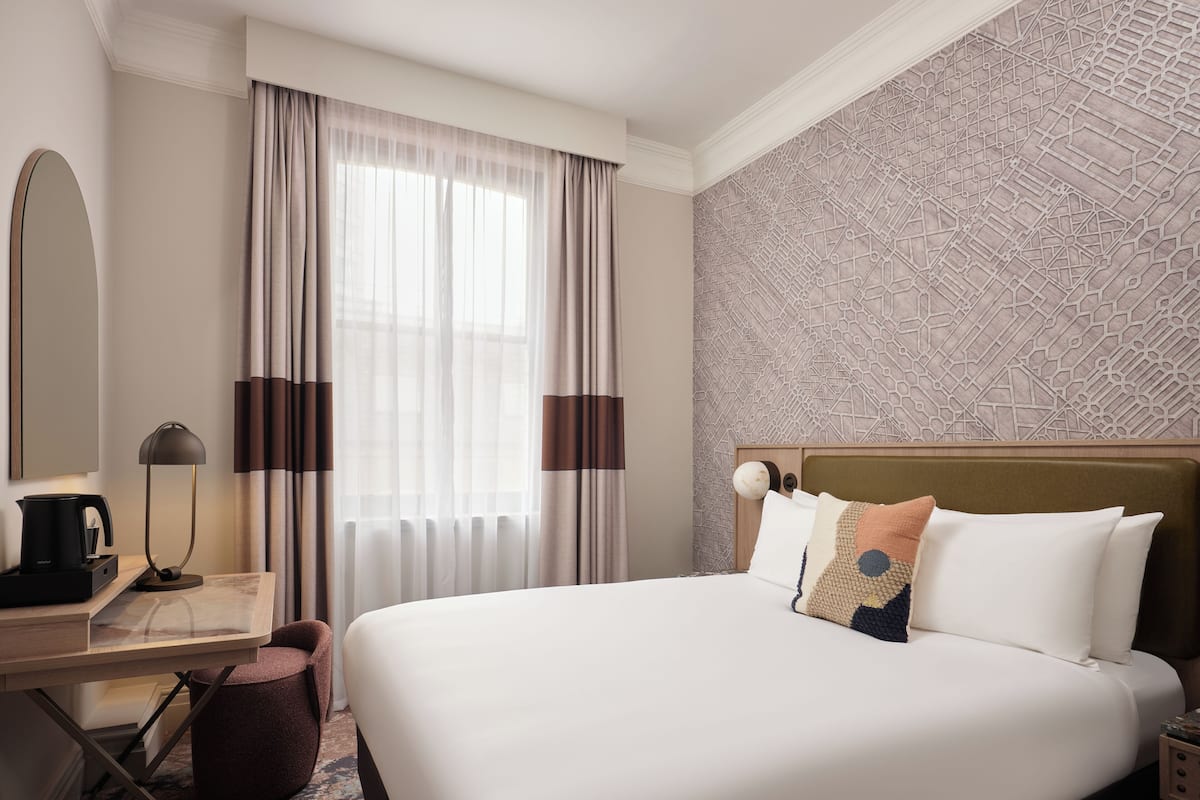Quarto de hotel com uma cama grande, uma escrivaninha com abajur, uma cafeteira e parede com padrão.