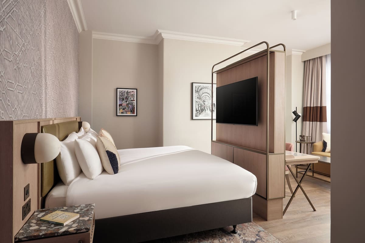 Quarto de hotel moderno com uma cama grande, televisão de tela plana, escrivaninha e um espaço de estar com luminária.