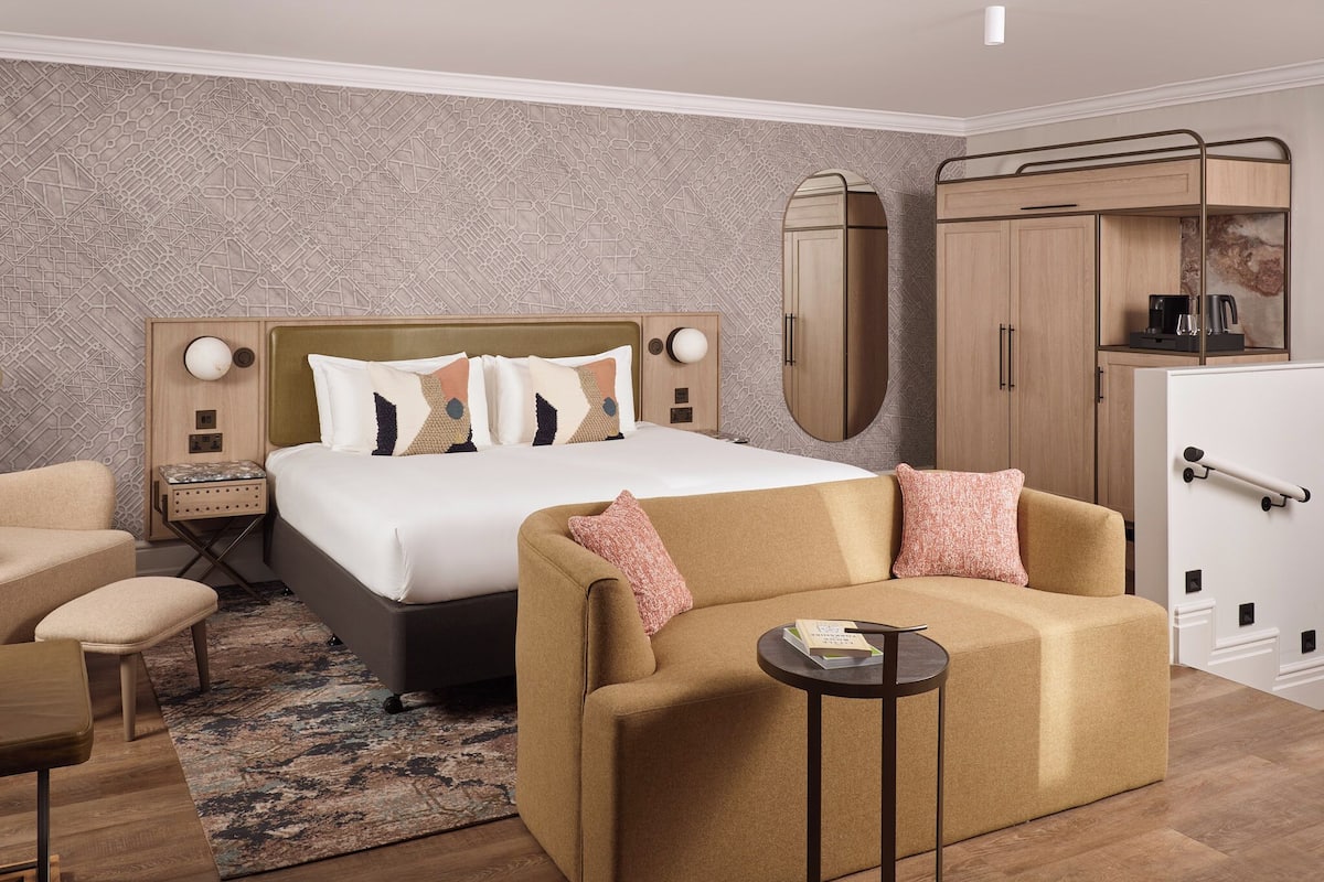 Quarto de hotel com cama, sofá, pequena mesa, guarda-roupa e espelho.